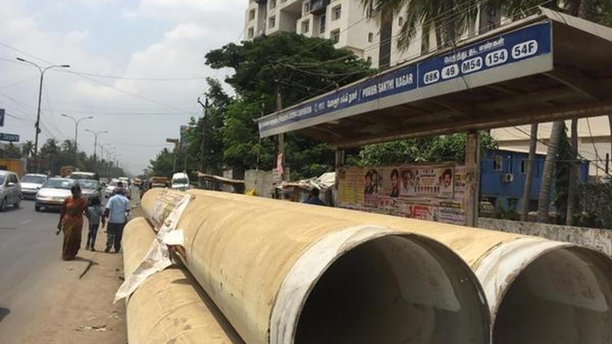 Pipes takes up commuters’ space at a bus stop in Porur - The Hindu